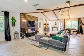 Uma sala de estar ampla, com uma televisão de tela plana grande, um sofá cinza e um espaço de jantar com mesa e cadeiras de madeira.