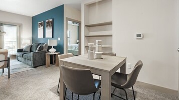 Uma sala de estar moderna com sofá, uma mesa de jantar com cadeiras e uma parede azul de destaque.