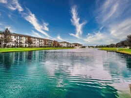 Um hotel à beira-mar com uma piscina refletora, uma área gramada e uma fileira de edifícios com varandas.