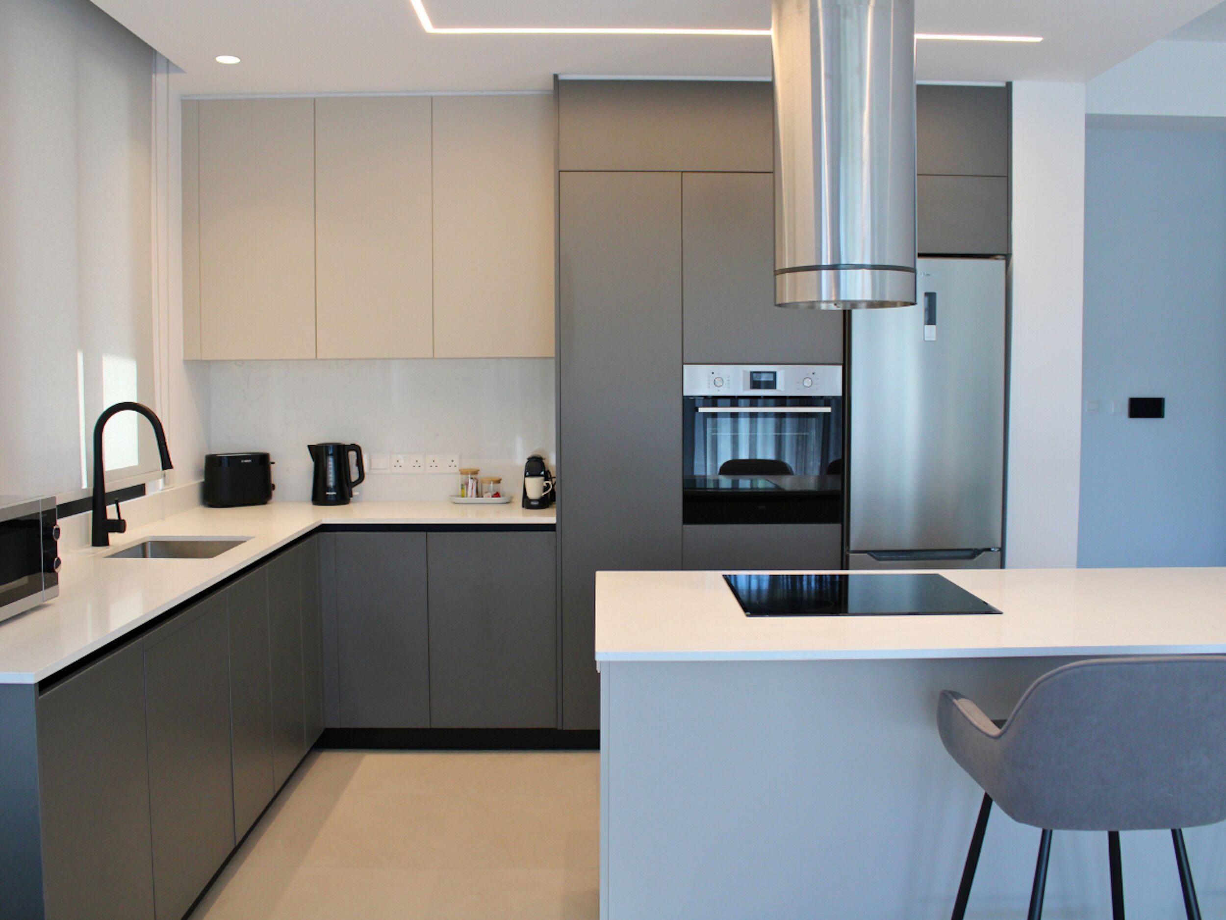 Cozinha moderna com ilha central, eletrodomésticos de aço inoxidável e uma cadeira cinza.