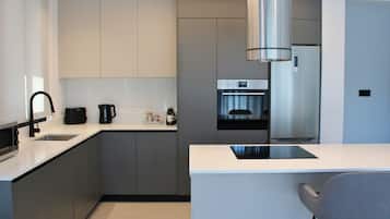 Cozinha moderna com ilha central, eletrodomésticos de aço inoxidável e uma cadeira cinza.