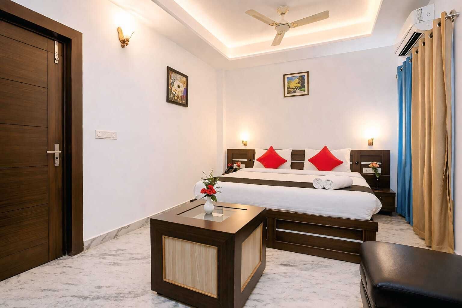 Quarto de hotel com cama, mesas de cabeceira, escrivaninha, ventoinha no teto e janela com cortinas.