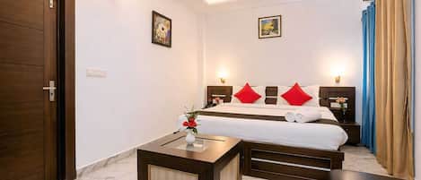 Quarto de hotel com cama, mesas de cabeceira, escrivaninha, ventoinha no teto e janela com cortinas.