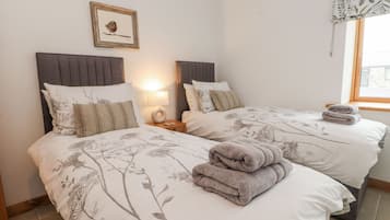 Quarto duplo com duas camas, cada uma com roupa de cama florida e cabeceira. Há uma mesinha de cabeceira com uma lâmpada e um quadro emoldurado na parede.