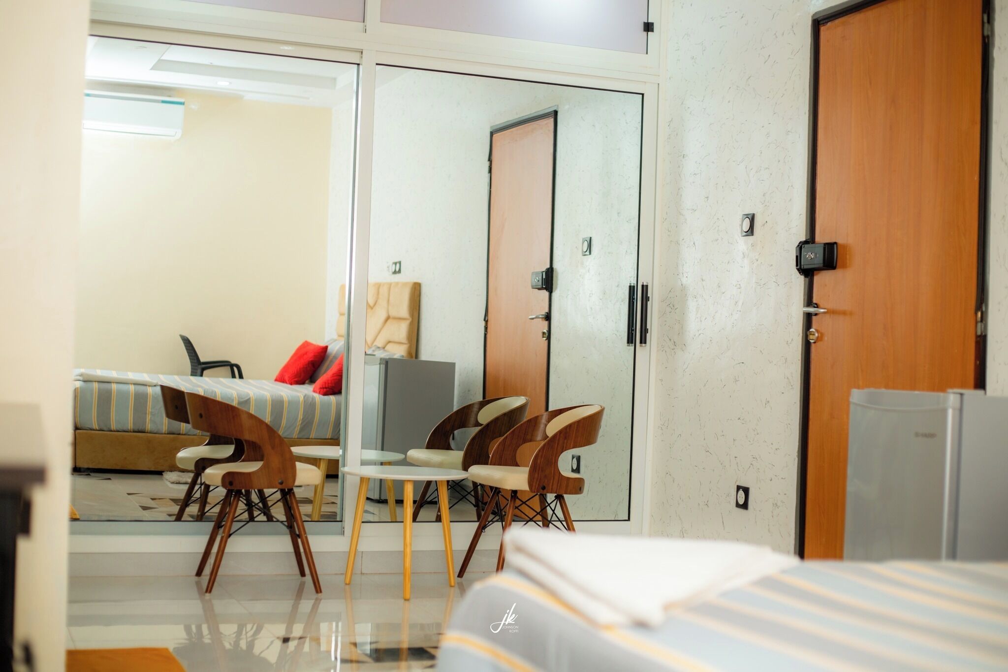 Quarto de hotel com cama, escrivaninha, duas cadeiras, sofá e porta deslizante que dá para outro cômodo.