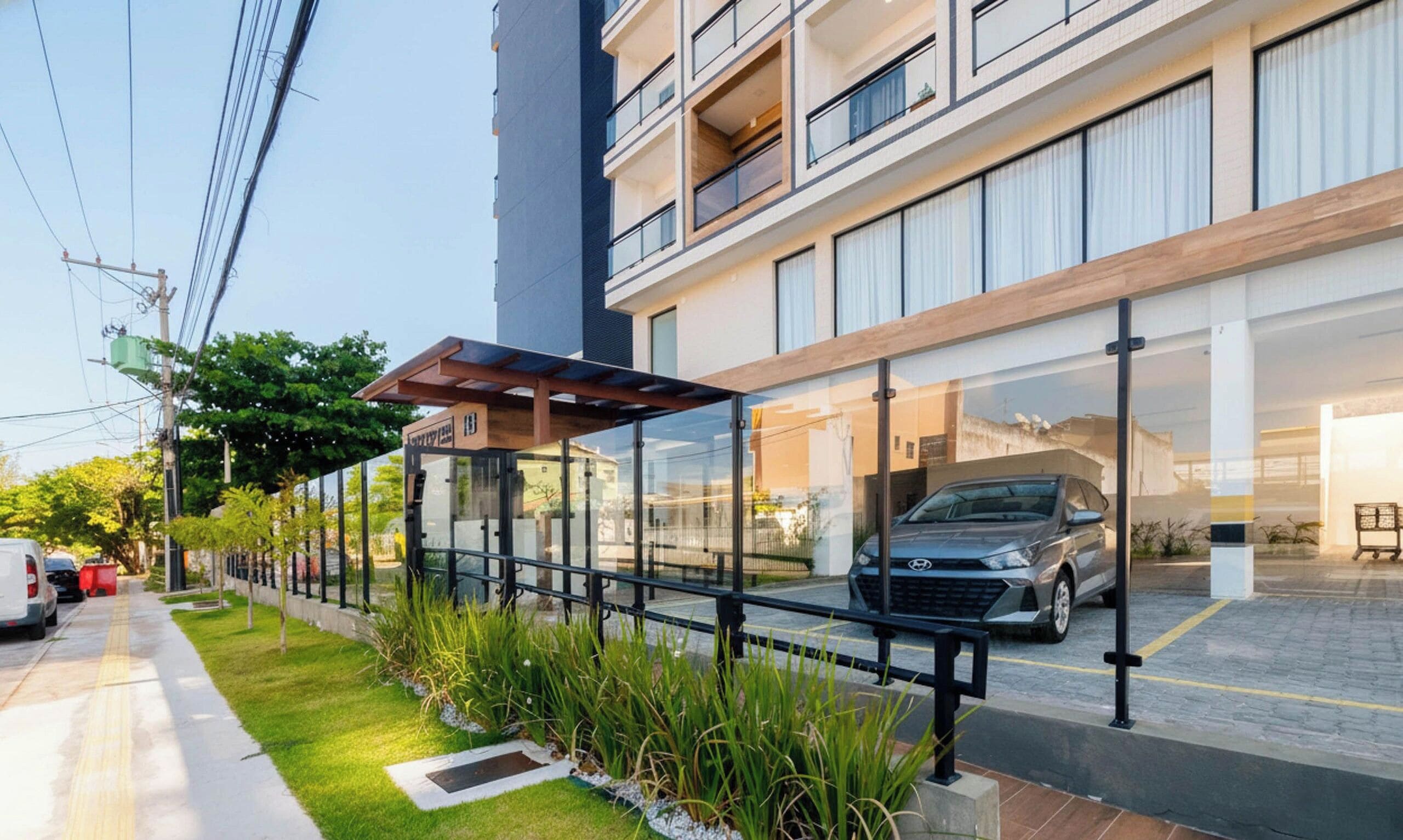 Um edifício moderno com área de estar coberta ao ar livre, um carro estacionado na frente e céu claro.