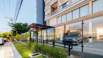 Um edifício moderno com área de estar coberta ao ar livre, um carro estacionado na frente e céu claro.