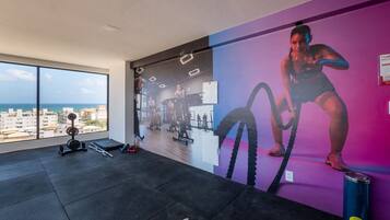 Uma academia com uma janela grande, equipamentos de exercício e um mural de uma pessoa se exercitando.