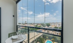 Varanda com guarda-corpo de vidro com vista para uma área residencial e uma piscina.