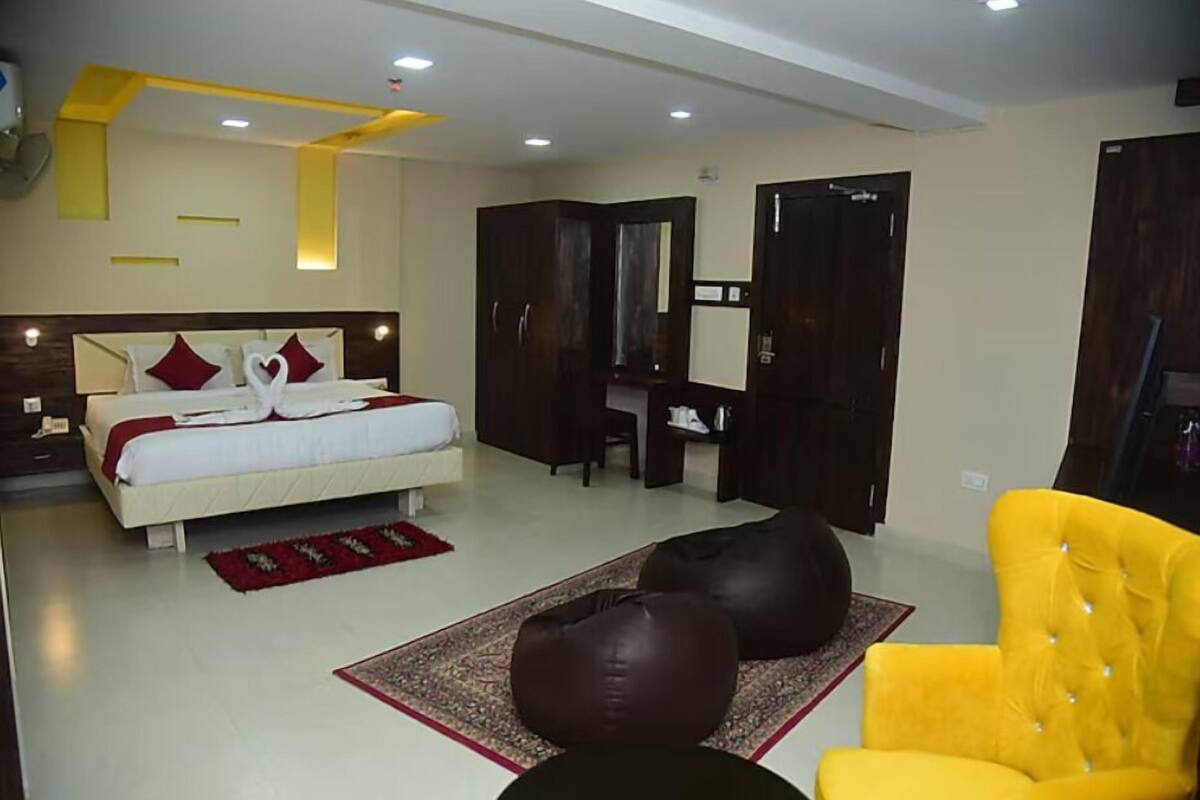 Quarto de hotel com cama, poltrona amarela, dois sacos de feijão, escrivaninha com cadeira e guarda-roupa.