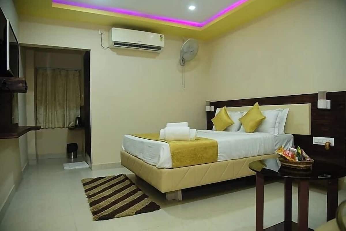 Quarto de hotel com cama, mesa de cabeceira, ar condicionado e ventilador.