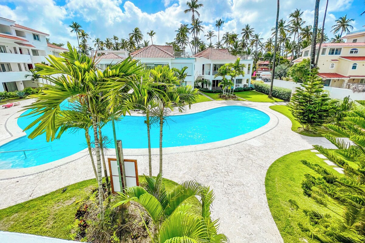 Resort com uma piscina grande, cercada por palmeiras e edifícios modernos.