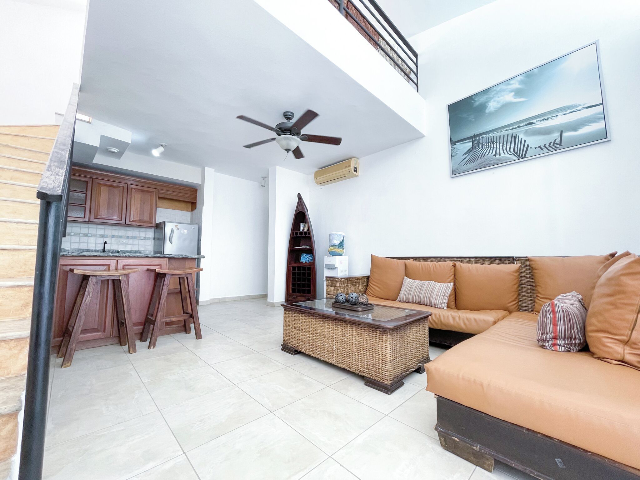 Uma sala de estar moderna com um sofá, uma mesa de centro e uma área de cozinha com armários de madeira e uma geladeira.
