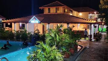 Um resort com piscina, um edifício bem iluminado e um calçadão pavimentado.