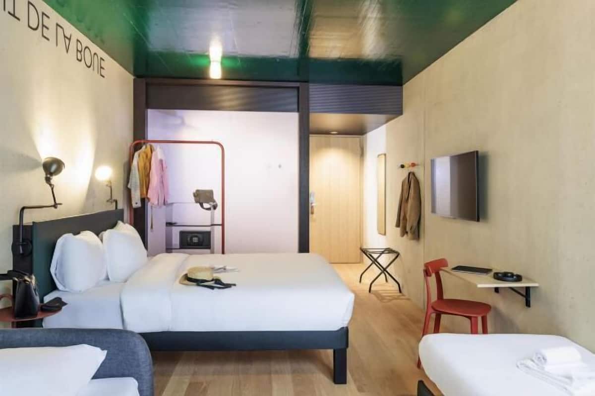 Quarto de hotel moderno com cama, mesa de cabeceira, luminária e televisão.