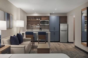 Quarto de hotel moderno com cozinha compacta, sofá, mesa de jantar e cama.