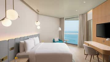 Quarto de hotel com cama, escrivaninha, cadeira, televisão e vista para o mar.