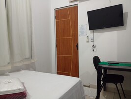 Quarto com cama, escrivaninha, cadeira, televisão e porta.
