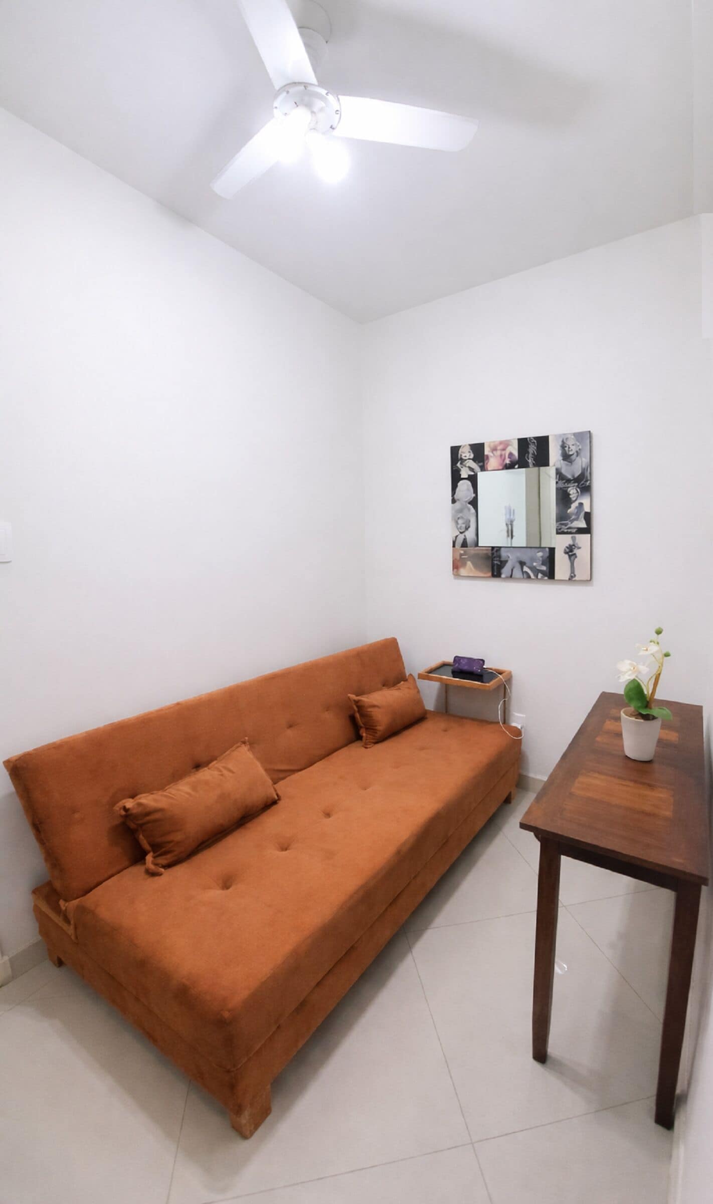 Quarto com sofá, mesa pequena, ventilador de teto e moldura de quadro na parede.