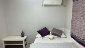 Quarto com cama, duas almofadas, mesa de cabeceira com abajur e ar condicionado na parede.
