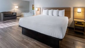 Quarto de hotel moderno com uma cama grande, um sofá, uma pequena mesa e uma luminária na parede.