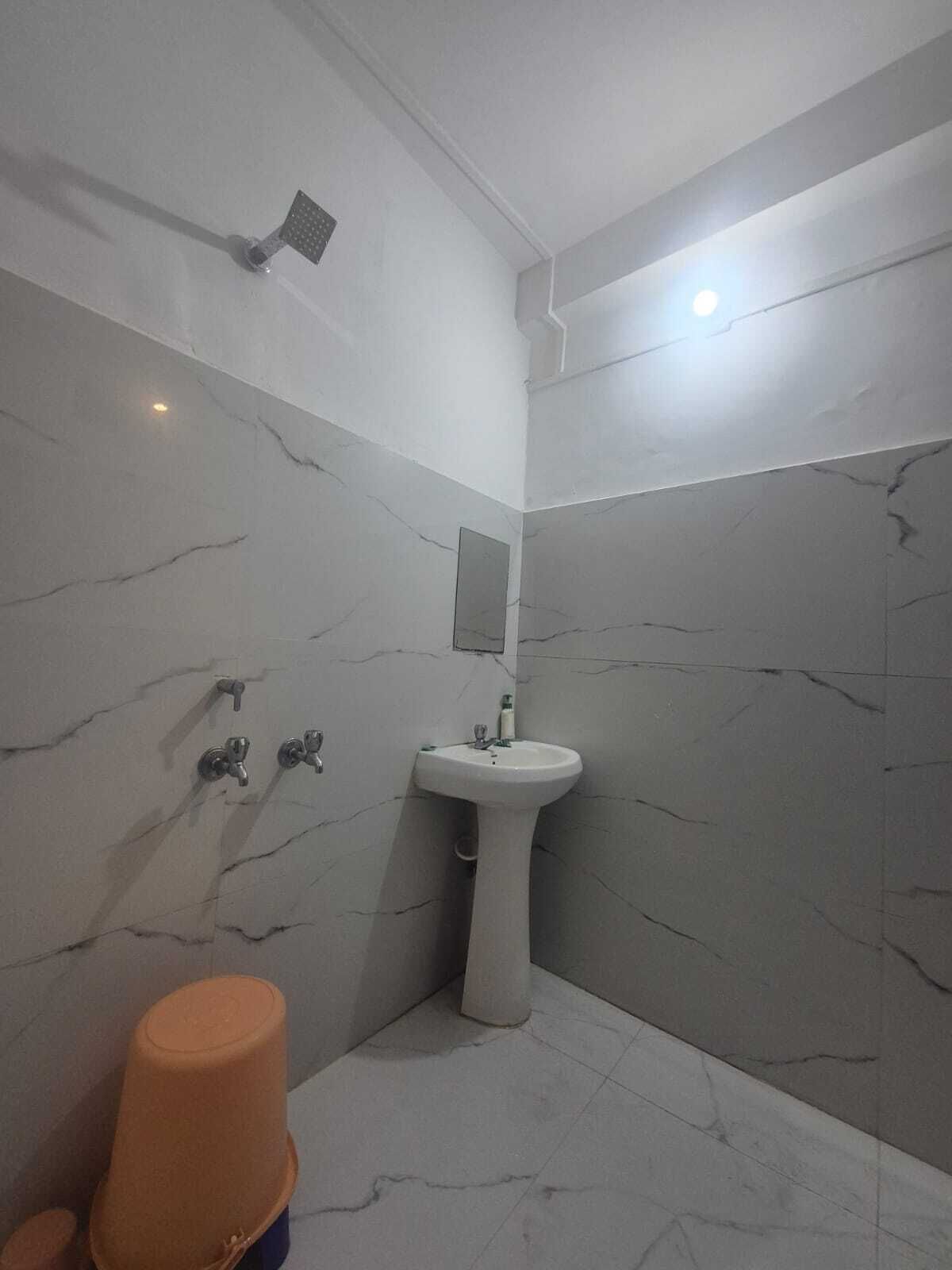 Um banheiro com uma pia de pedestal branca, um espelho acima dela e um vaso sanitário com uma lixeira.