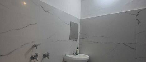 Um banheiro com uma pia de pedestal branca, um espelho acima dela e um vaso sanitário com uma lixeira.