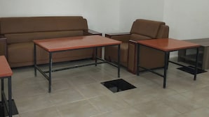 Um quarto com um sofá marrom, duas mesas vermelhas e um tapete de chão preto.