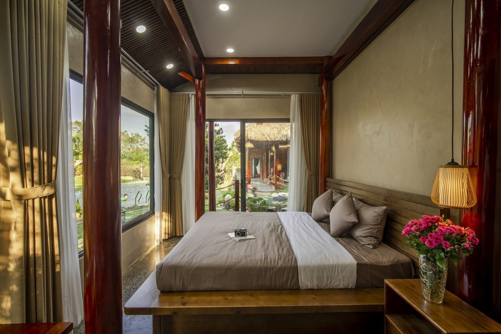 Quarto com cama, mesa de cabeceira, abajur e vista para a piscina e jardim.