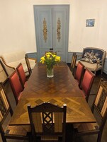 Uma sala de jantar com uma longa mesa de madeira, cadeiras estofadas vermelhas e um vaso de flores amarelas.