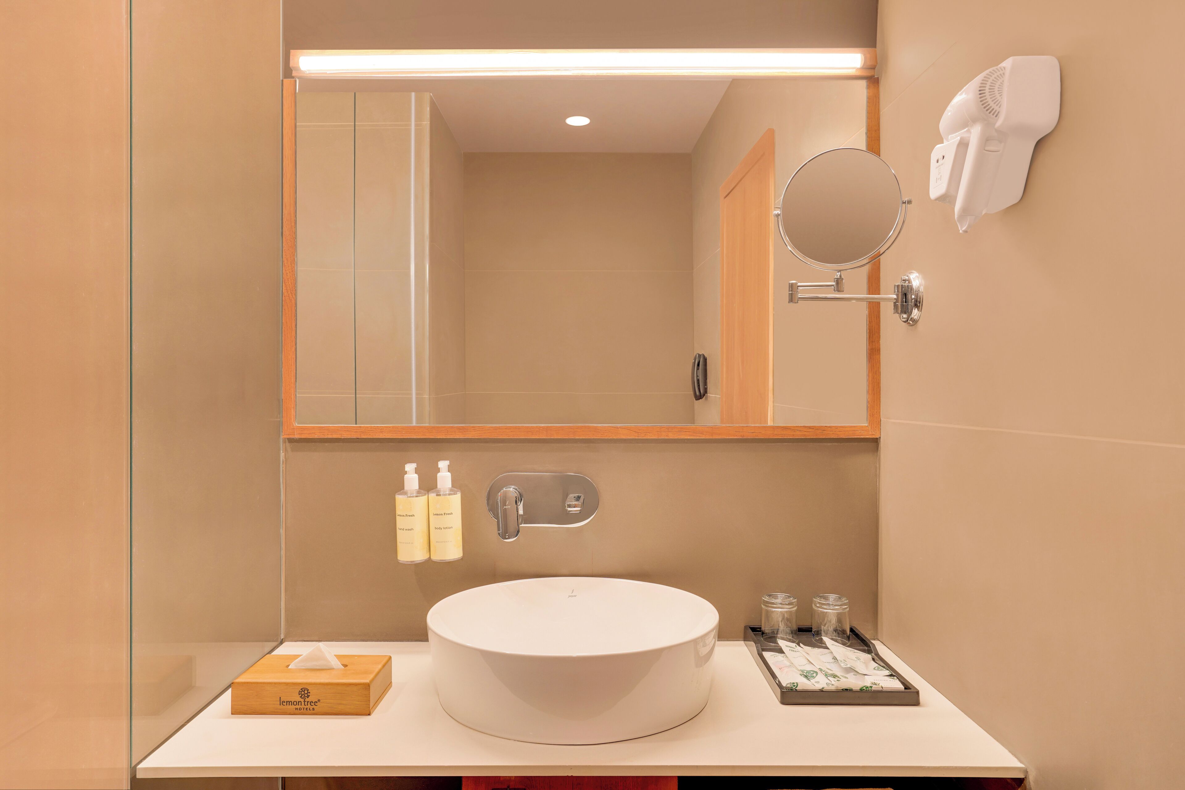 Casa de banho com lavatório redondo, espelho, secador de cabelo e produtos de higiene na parede.