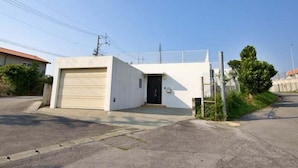 Um pequeno edifício térreo com uma porta de garagem, uma porta preta e uma pequena varanda.