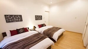Quarto de hotel com duas camas, cada uma com manta marrom e roupa de cama branca. Duas obras de arte estão penduradas na parede acima das camas.