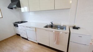 Uma cozinha com armários brancos, pia de aço inoxidável, fogão a gás e geladeira.