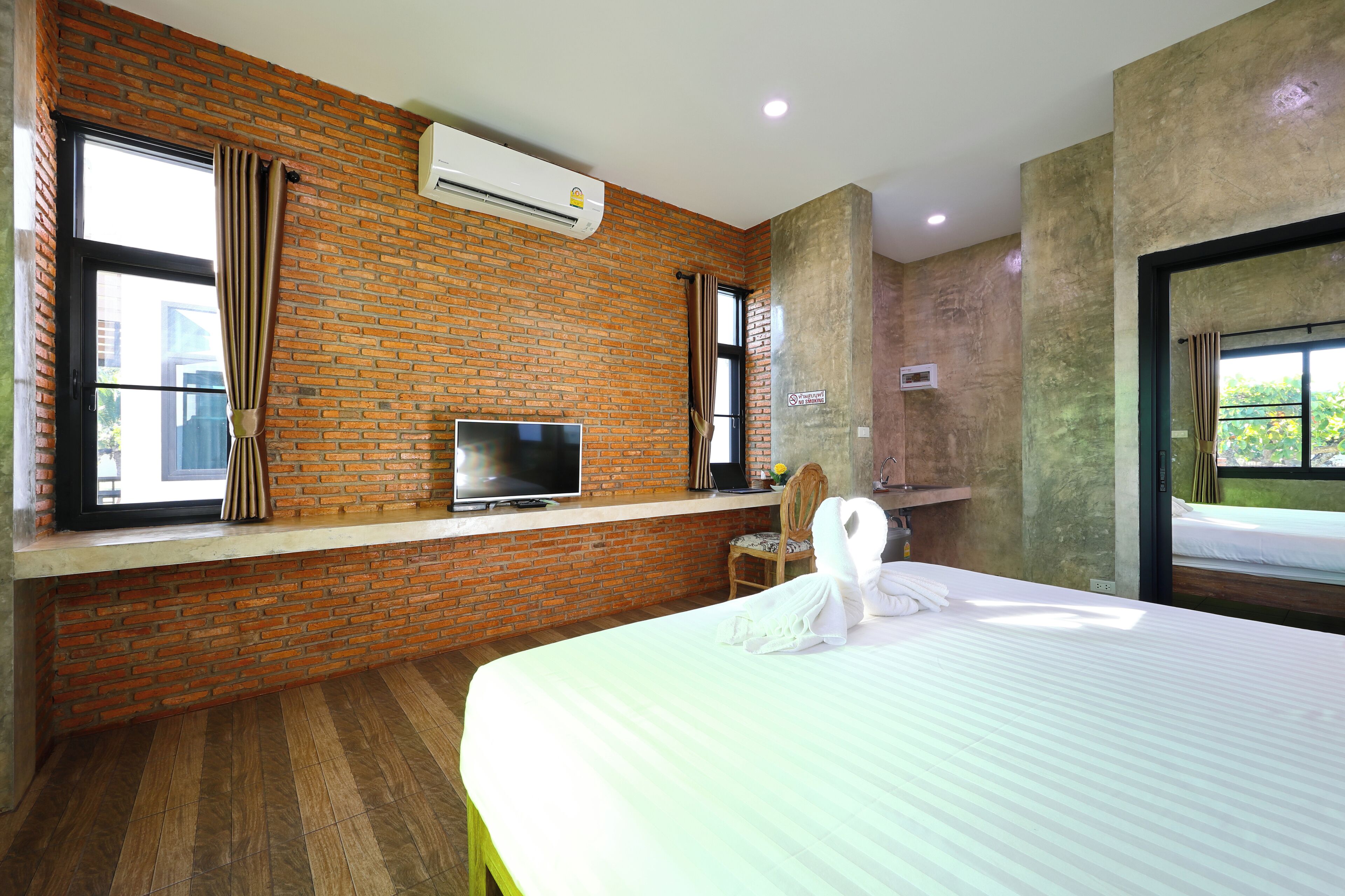 Quarto de hotel com parede de tijolos, televisão de tela plana, cama com edredom branco e janela com cortinas.