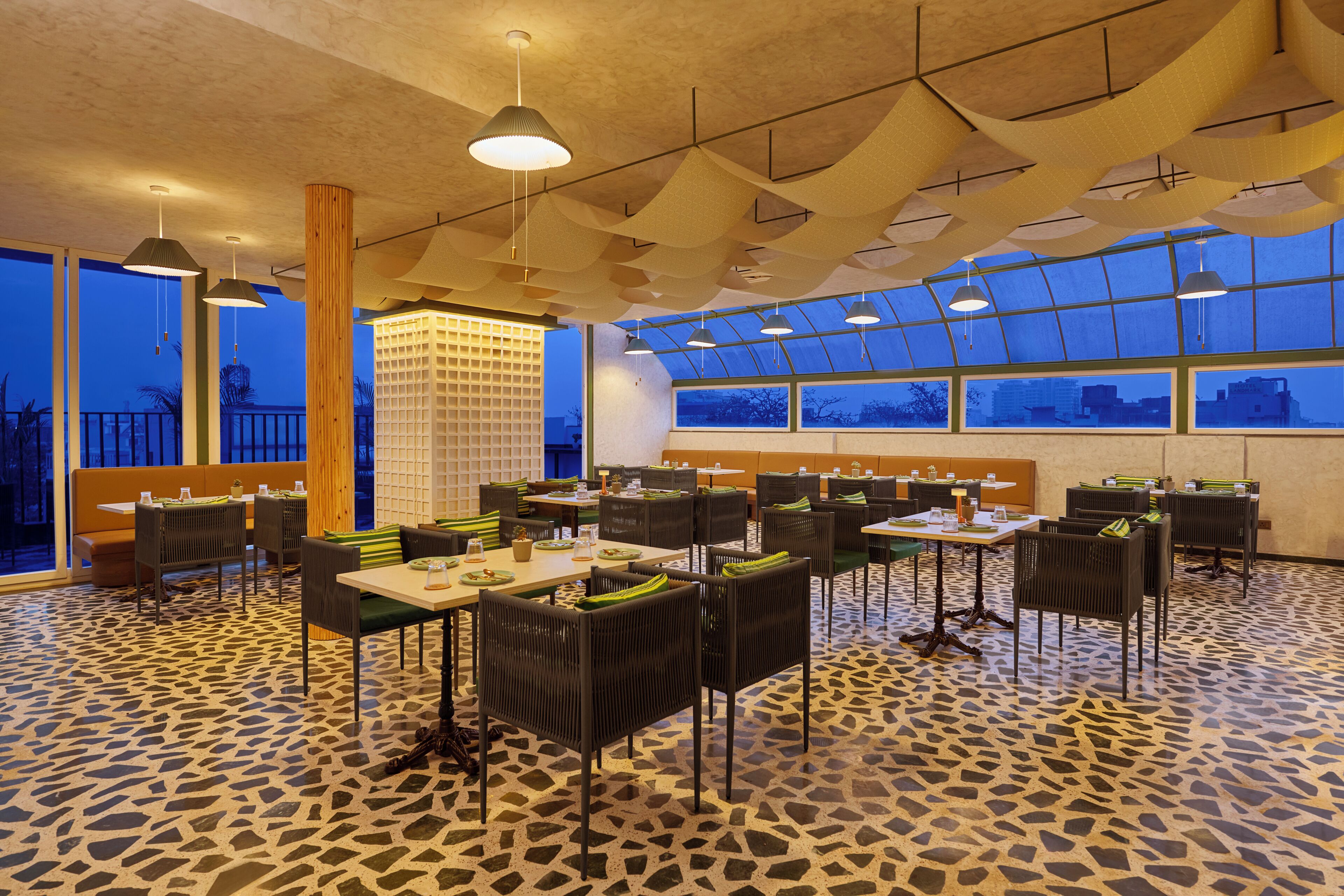 Um restaurante com mesas, cadeiras, piso estampado e grandes janelas.