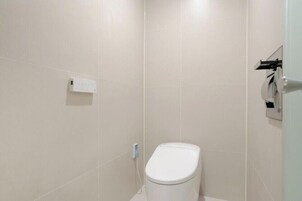 Casa de banho pequena e moderna com sanita, tomada elétrica na parede e dispensador de papel.