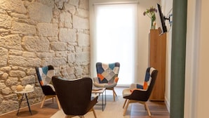 Uma sala de estar moderna com parede de pedra, duas poltronas estampadas, um sofá escuro e um armário de madeira.