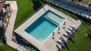Vista aérea de uma piscina retangular com deck revestido de azulejos, cercada por um gramado bem cuidado e uma parede de pedra.