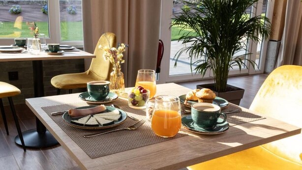 Mesa de café da manhã posta com pratos, talheres e um copo de suco de laranja.