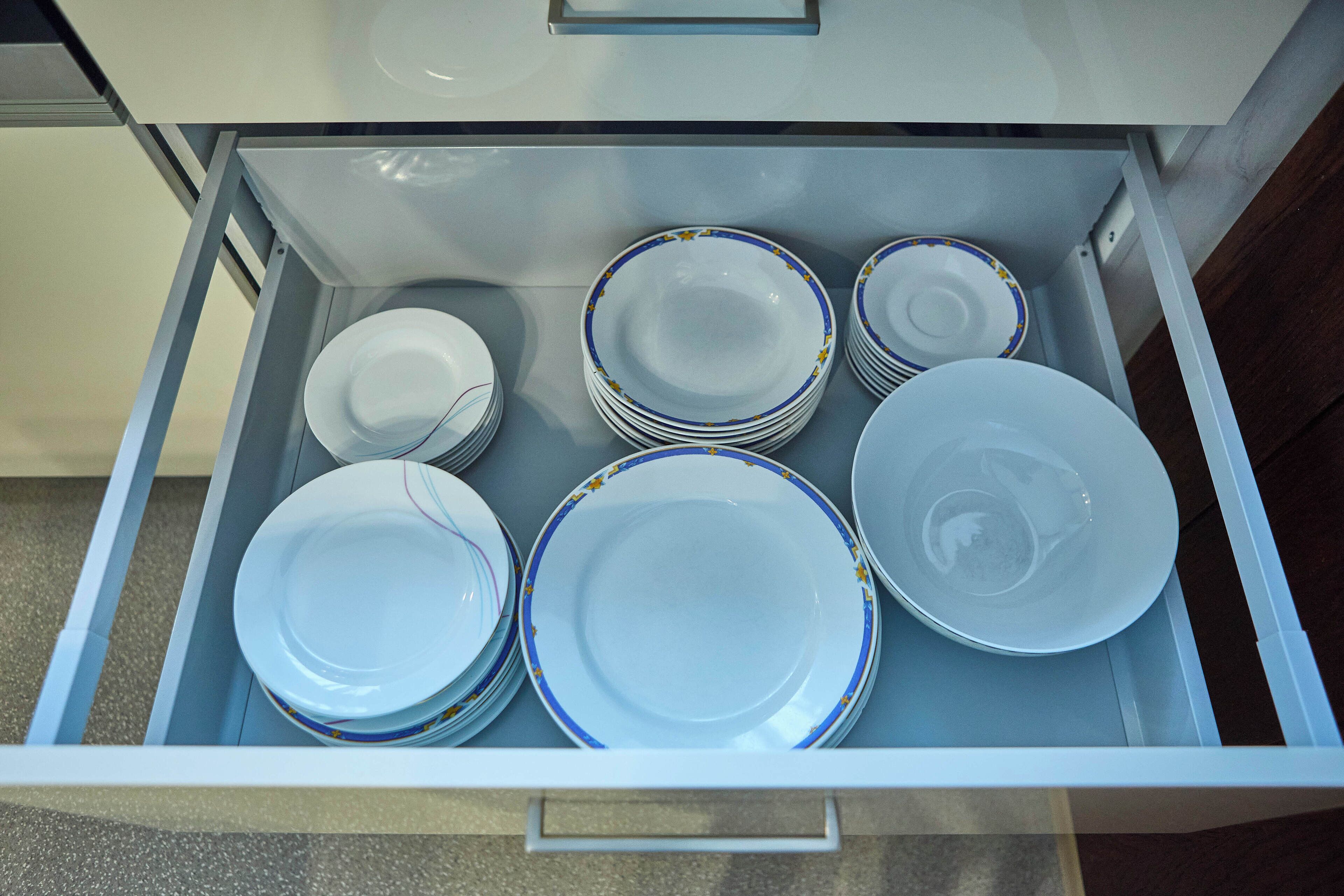 Uma gaveta com pilhas organizadas de pratos com borda azul e padrão floral amarelo.