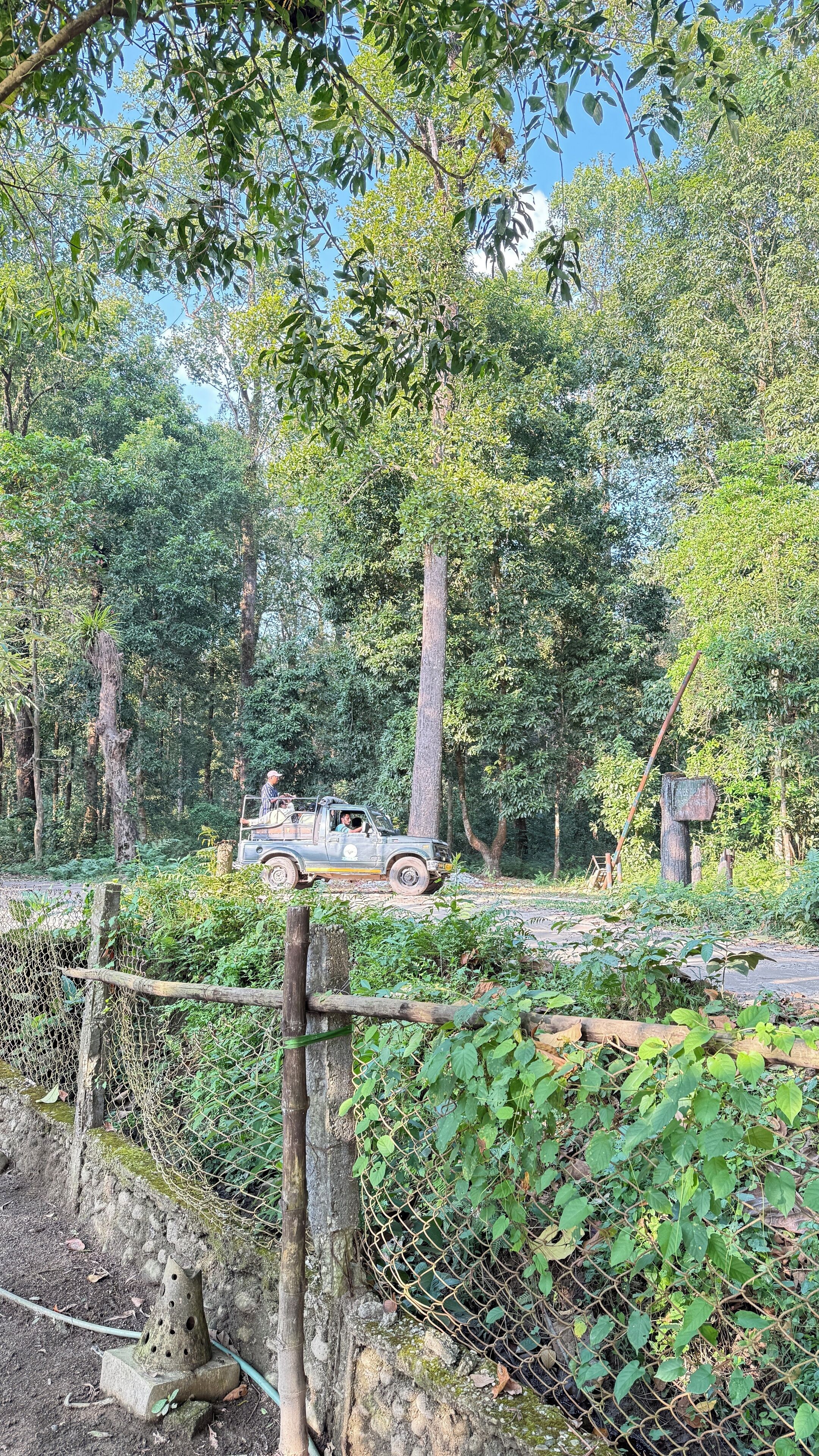 Um veículo estacionado em área arborizada, com cerca de arame e poste de concreto com buracos.