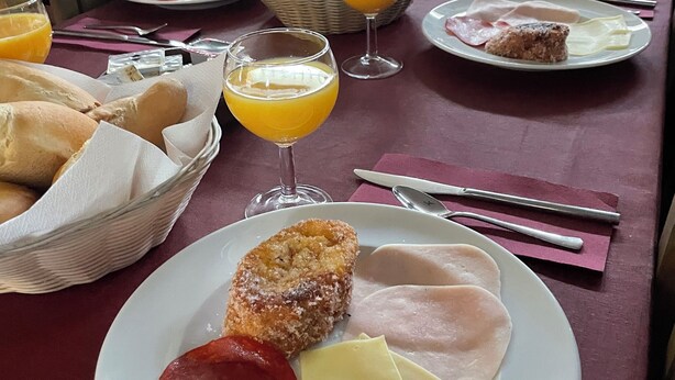 Mesa posta com pratos de comida, copos de suco de laranja e cestas de pão.