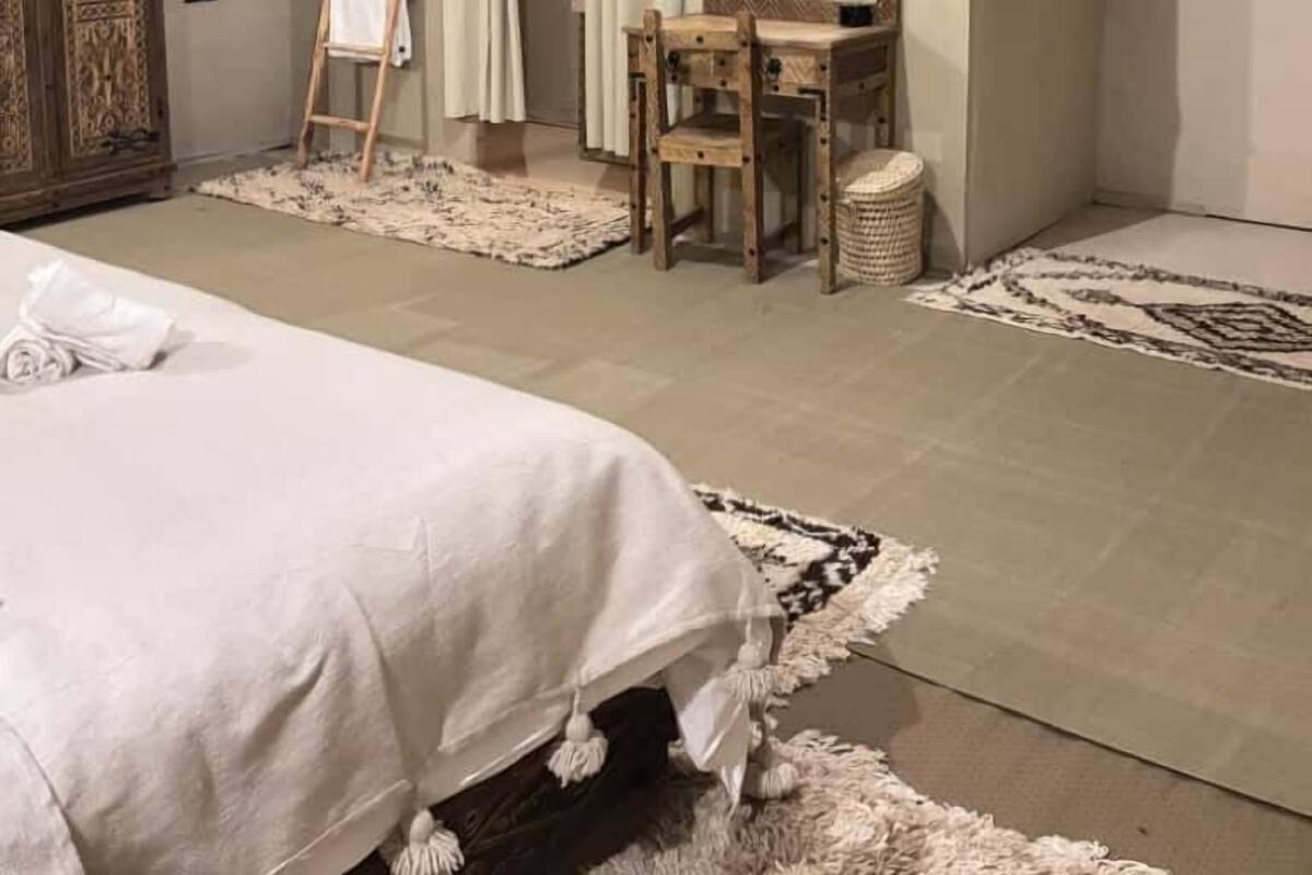 Quarto com cama, cómoda de madeira, espelho e uma pequena mesa com cadeira.
