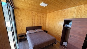 Quarto com teto de madeira, cama com colcha marrom, mesa de cabeceira e guarda-roupa.