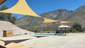 Uma área de piscina com deck de madeira, balanço e um gazebo branco.