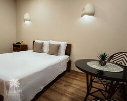 Quarto com cama, mesa de cabeceira, luminária e uma pequena mesa redonda com decoração de abacaxi.