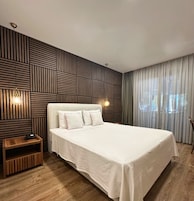 Quarto de hotel moderno com uma cama grande, parede de painéis de madeira e uma mesa de cabeceira.