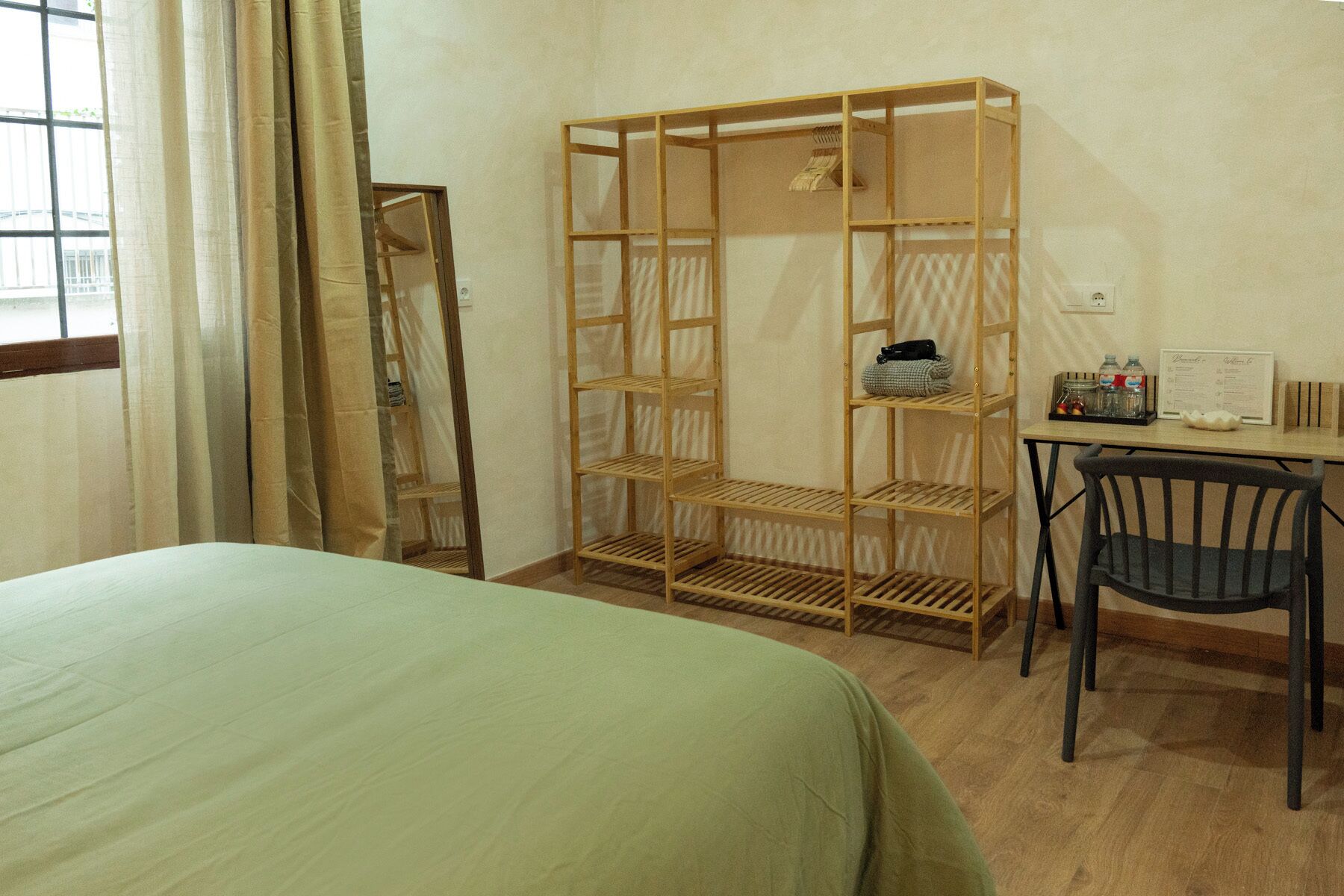 Quarto com cama, estante de madeira, escrivaninha com cadeira e janela com cortinas.