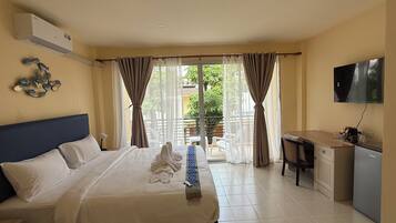 Quarto de hotel com cama, escrivaninha, televisão e varanda com cortinas.